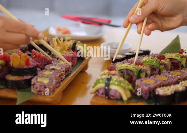 Sushi dinner. Side view of two hands picking up sushi rolls with ...