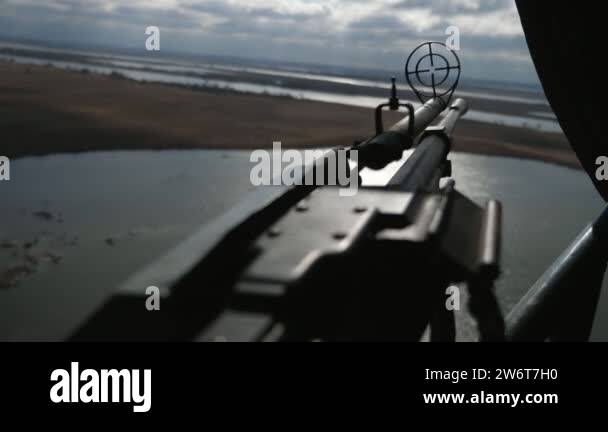 Large machine gun with a round front sight is aimed at a lake from a ...
