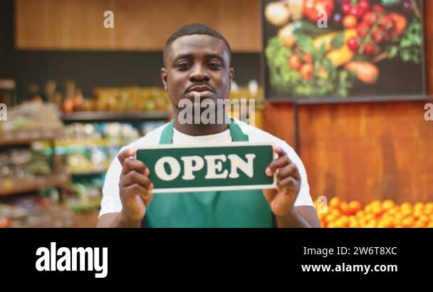 Handsome young guy standing behind seller stall and holding board in ...