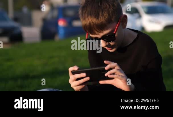 Schoolboy using a smartphone sitting on the lawn. Generation Z. Boy ...