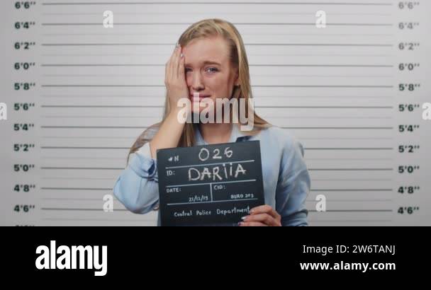 Mugshot of arrested young woman crying while holding sign for photo in ...