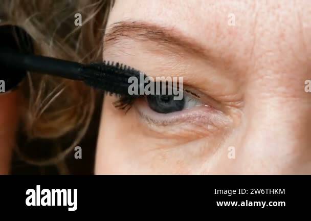 closeup footage of a middle-aged woman doing corrective eye makeup to ...