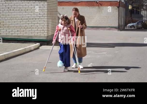 Mom Helps Her Daughter Learn To Walk On Crutches Plaster On Your Feet