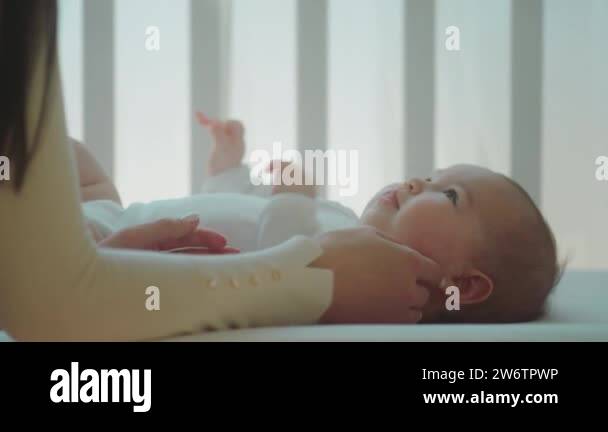 Pretty baby girl laying down on her baby cot her mother playing ...