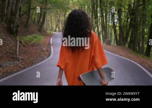 skateboarder is walking alone in forest park at summer, sporty woman is ...