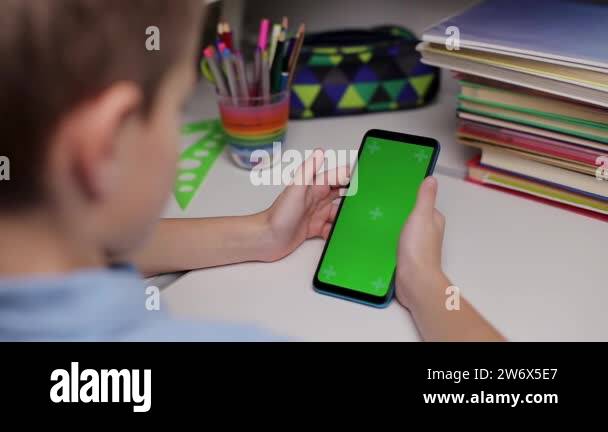 Boy holding a smartphone with a green screen at home, scrolling ...