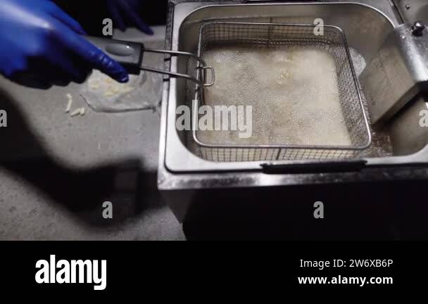 Chunks of French fries are fried in boiling oil in the kitchen. The ...