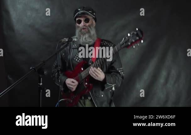 Rockstar bearded in leather jacket and cap wearing round sunglasses ...