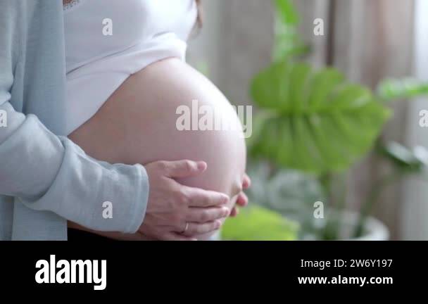 4k Pregnant mother holding baby clothes in hands. Happy Expectant ...