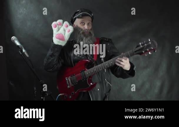 Bearded rocker in leather jacket and cap smiling and waving to audience ...