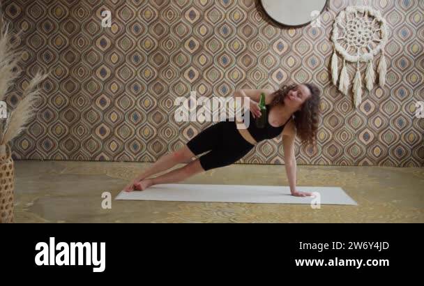 Beer yoga. Curly-Haired Young woman doing yoga stretching exercise with a bottle of beer. Sporty ...
