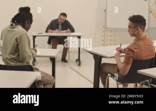 Rear view of two male students sitting across isle between school desks ...