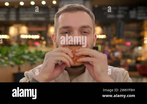 Unshaven caucasian man eats meat burger with pleasure, bites burger ...