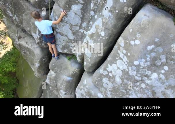 Determined boy climber clambering up steep wall of rocky mountain ...