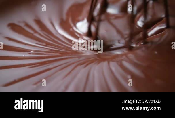 Close-up chocolatier mixing melted liquid chocolate with steel whisk ...