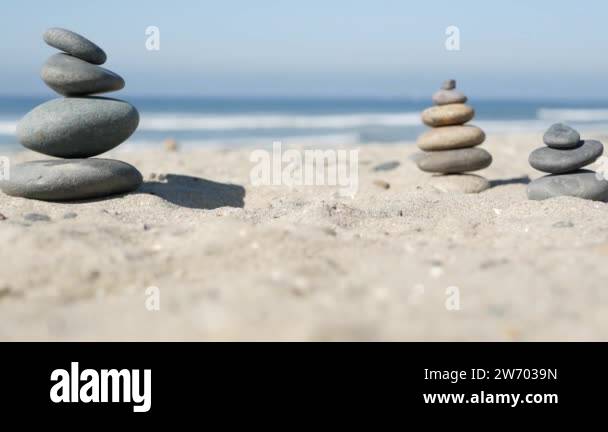 Rock balancing on ocean beach, stones stacking by sea water waves ...