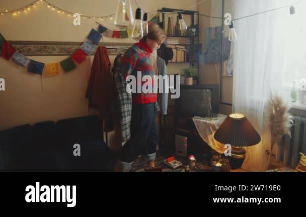 PAN shot of young man entering room, taking off jacket, jumping on bed ...