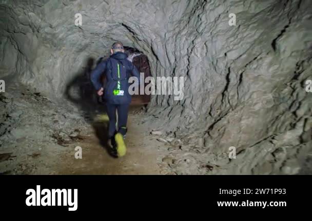Two Caucasian men running inside narrow rock tunnel in underground cave ...