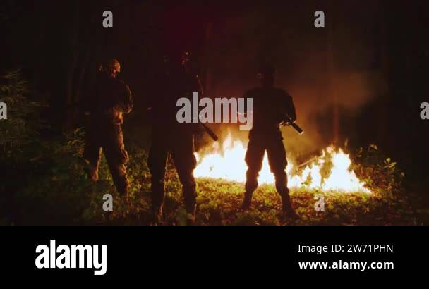 Backlit silhouette of special forces marine operators in forest on fire ...