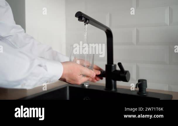 Man fills an empty glass with drinking water in the kitchen. Water ...