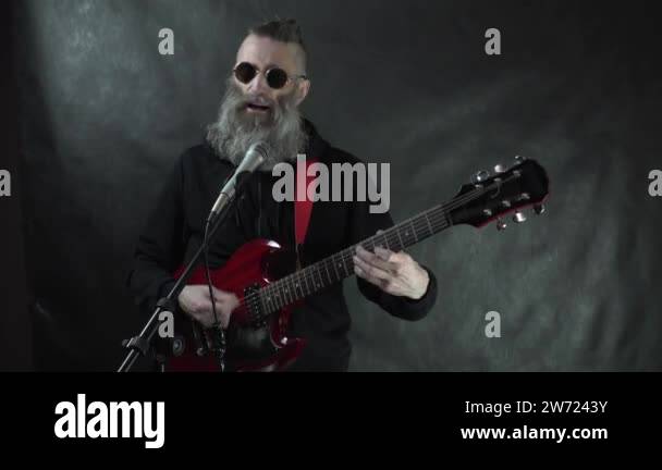 Bearded rocker with shaved temples in black hoodie and round glasses ...
