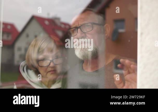 Husband and wife, an elderly couple looks out the window and is sad ...