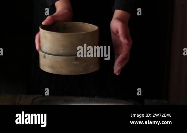 Sieving whole wheat flour through old sieve by woman's hands. Dark ...