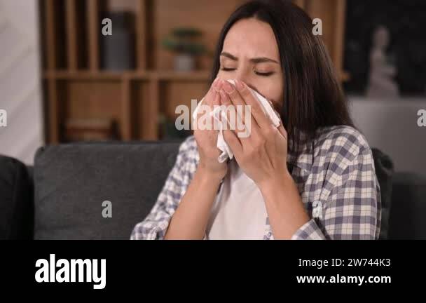 Sick caucasian young adult woman sit on a couch in living room, feel ...
