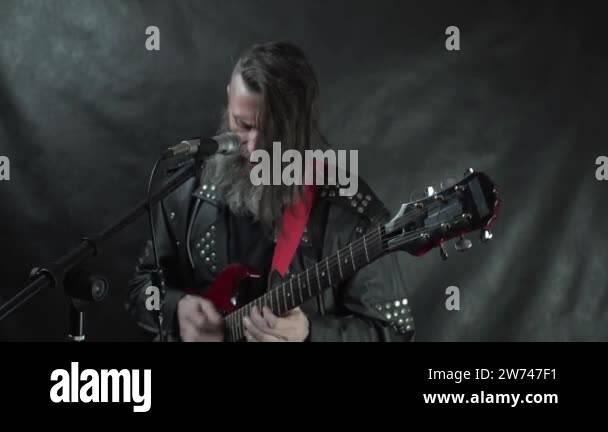 Bearded long-haired rock musician in leather jacket plays red electric ...