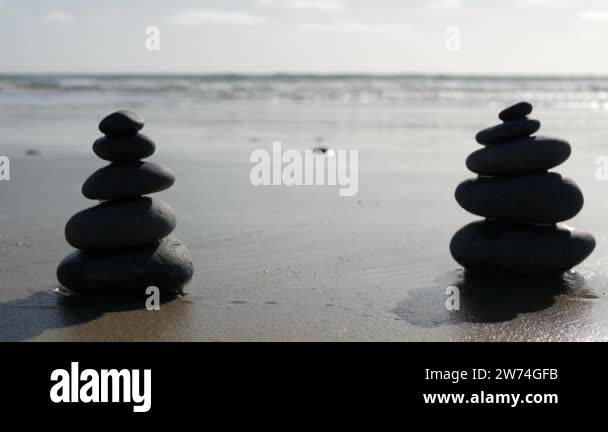 Rock balancing on ocean beach, stones stacking by sea water waves ...