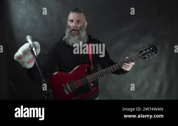 Punk rockstar with shaved temples, beard and black hoodie plays by cat ...