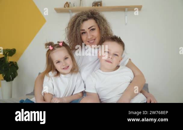 Daughter and son sit in moms arms and kiss moms cheeks. Family in a ...