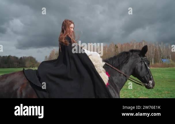 Beautiful female in a medieval dress riding a horse through a ...