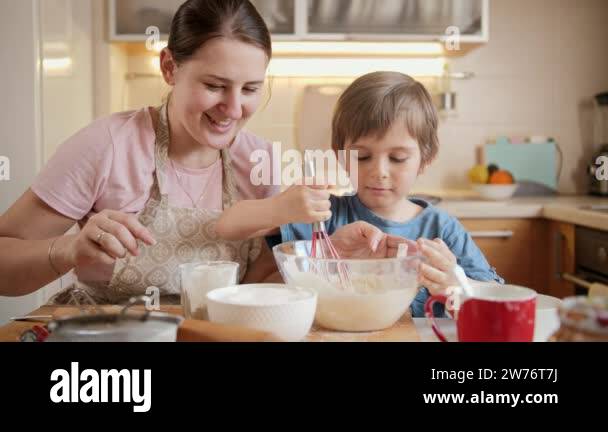 Young smiling mother cooking with little son and sifting flour with ...