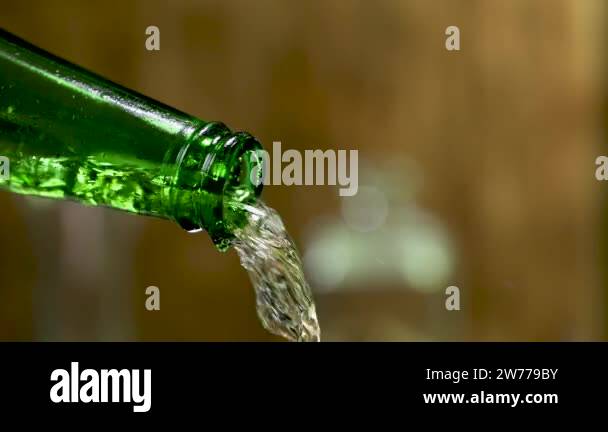 Stream of cold, fresh beer pours from a green, misted bottle. Splashes ...