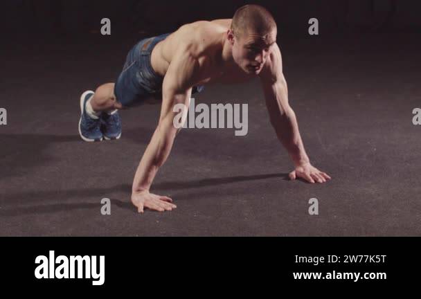 Young pumped-up guy in denim shorts doing stamina exercises for his arms and shoulders - push ...