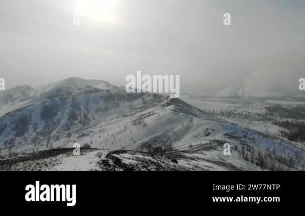 Aerial view of factory. The winter hills are covered with snow. Behind ...