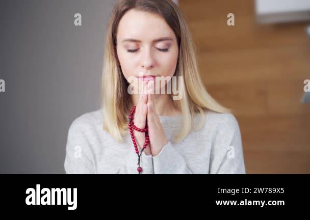 portrait young girl or woman sincerely praying on rosary at home ...
