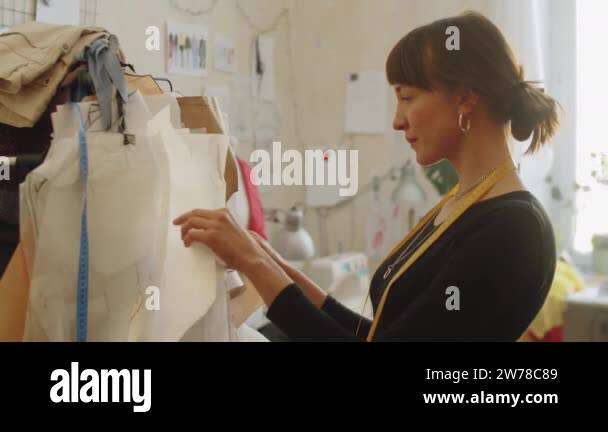 Female dressmaker with measuring tape over neck walking to rack in ...