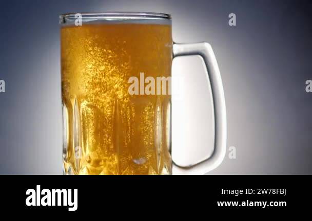 Light foamy beer is poured into a glass half-liter mug on a lighted ...