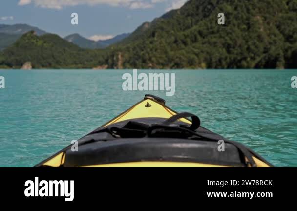 A front of yellow kayak slowly turning on an emerald lake overviewing ...