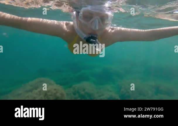 A slender young woman swims in a scuba mask and snorkel underwater in a ...