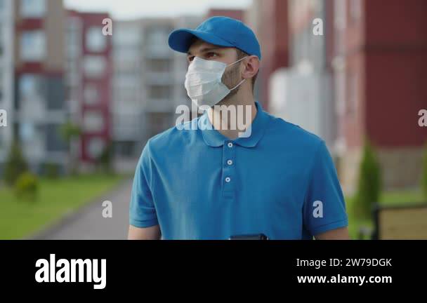 An young mailman courier with a protective mask and gloves is ...