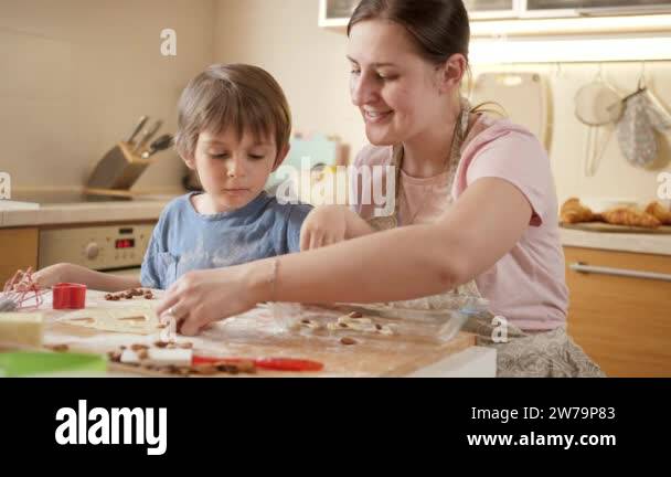 Happy smiling boy with mother making biscuits and putting them in ...