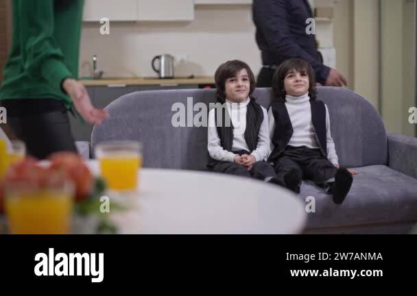 Middle Eastern twin brothers sitting on couch watching TV as couple of ...