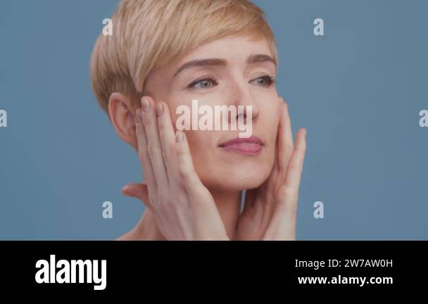 Semi profile portrait of middle aged blonde lady massaging face and ...