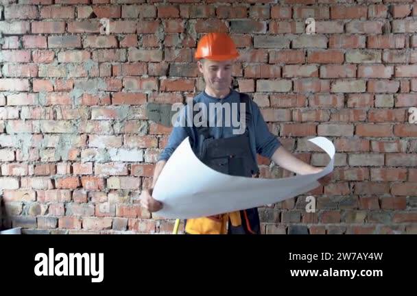 A man builder, dressed in an orange hard hat and uniform, and goggles ...