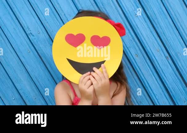 A cute little girl covers her face with a cardboard smiley face with ...