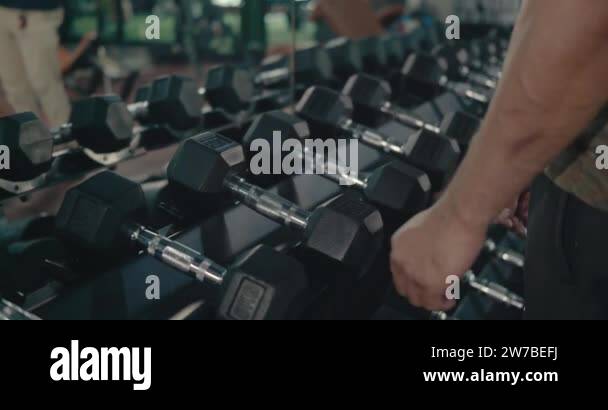 Close up man hands bodybuilder picking up or choosing dumbbell that are ...