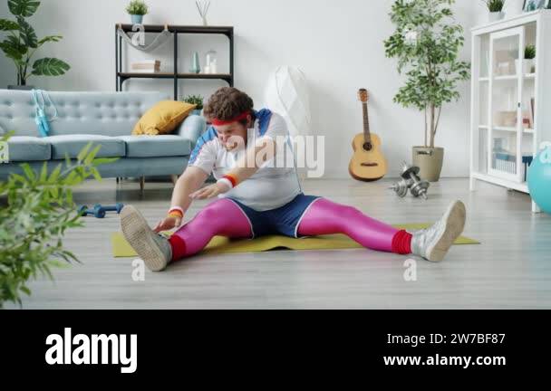 Awkward overweight young man in bright outfit stretching legs and arms ...